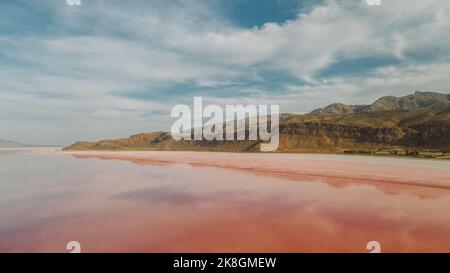 Pink water of Maharloo lake located near mountain ridge against cloudy ...