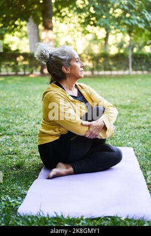 Elderly woman doing twisting asana Parivritta Parsvakonasana in yoga ...