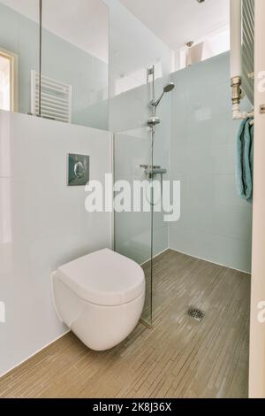 Flush toilet located between sink and shower in small tiled bathroom of ...