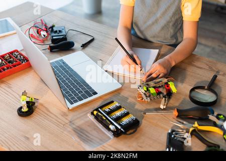 cropped view of girl near gadgets and vegetables holding plastic fork ...