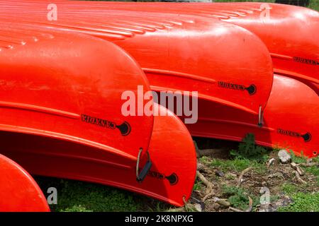 prow bow of red green canoe kayak neatly stacked inverted laid on grass ...