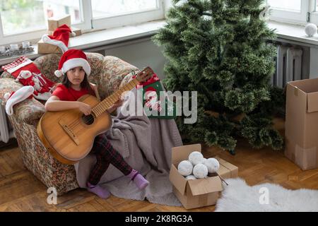 Child playing the guitar and singing near a christmas tree Stock Photo ...