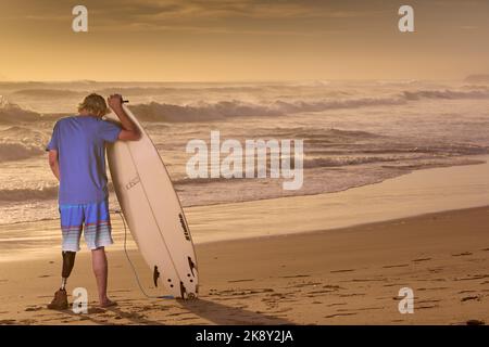 One legged disabled surfer wearing prosthetic leg on beach looking at ...