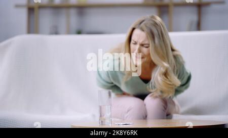 blonde woman suffering from period pain near glass of water and bottle ...