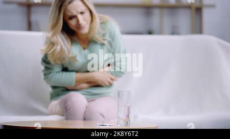 blonde woman suffering from period pain near glass of water and bottle ...
