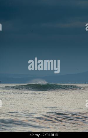 A vertical shot of foamy ocean waves hitting the big coastal rocks ...
