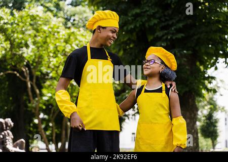 African children cooks in chefs hat and yellow uniforms smiling outdoor ...