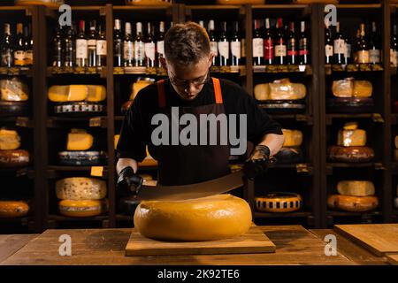 Cheese sommelier cutting yellow cheese wheel cut in half with a knife ...