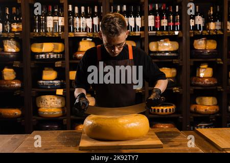 Cheese sommelier cutting yellow cheese wheel cut in half with a knife ...