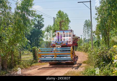 A man sits on a rice harvesting machine on a small rural road in ...