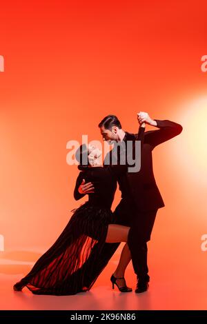 Side view of ballroom dancers performing tango on grey background with ...