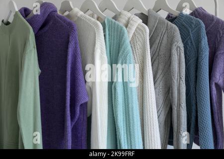 Rack with knitted sweaters near light wall in room Stock Photo - Alamy