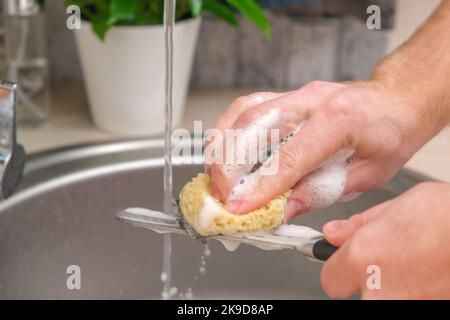 A man washes a sharp steel dirty kitchen knife with a sponge with ...