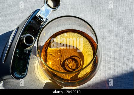 Black and silver whiskey flask next to a glass of amber colored liquid ...