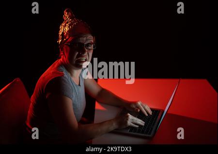 Paranoid caucasian woman typing on a computer wearing a tinfoil cap ...