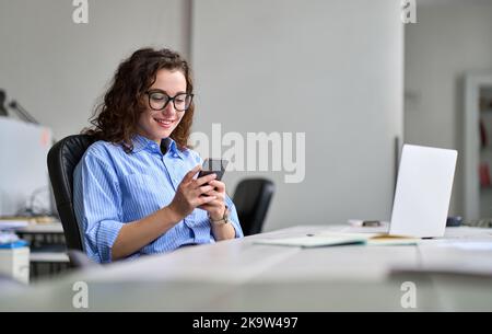 Smiling woman sitting at desk with smartphone and peonies, modern home ...