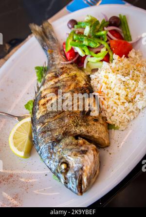 A whole grilled sea bream with rice and salad from a Greece local ...
