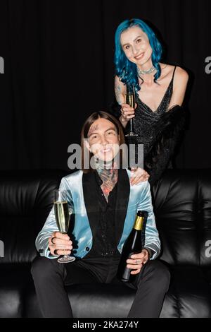elegant nonbinary friends with champagne smiling at camera near disco ...