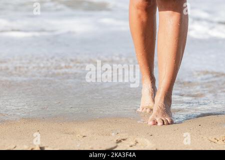 Crop anonymous barefoot woman walking on sandy beach along waving sea ...