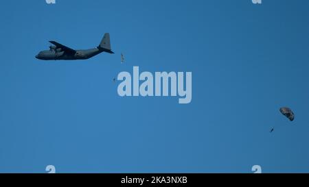A military personnel parachuting from a RAAF aircraft in blue sky ...