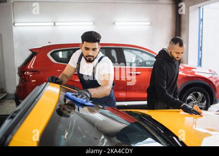 Car wash team cleaning a vehicle and a female worker with a bucket ...