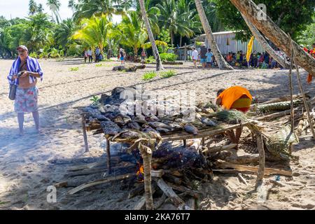 Locals preparing and cooking fish on open fire on beach, Kiriwina ...