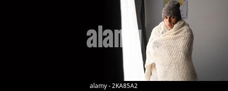 Unwell male renter in hat and jacket sit in cold living room suffer ...