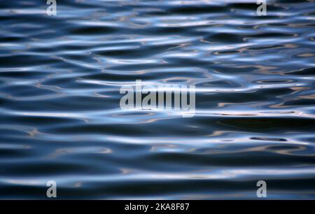 Closeup of calm river water surface with water splashes in blue color ...