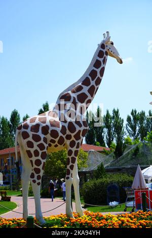 Plastic giraffe statue at park with colorful flowers in a sunny day ...