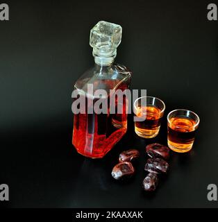 Date liqueur, strong homemade alcohol and dried fruits on a black ...