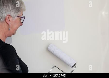 Mature woman starting to use paint roller on a wall Stock Photo - Alamy