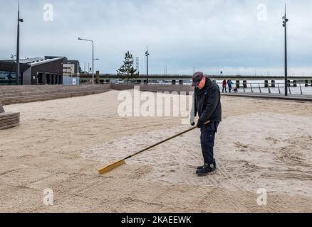 Maintenance workman raking sand on urban beach, Dundee Waterfront or ...