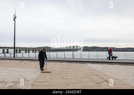 Maintenance workman raking sand on urban beach, Dundee Waterfront or ...