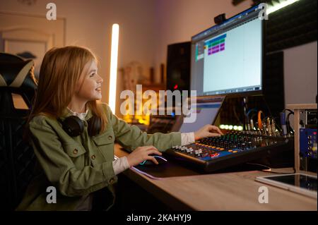 Young sound producer preteen girl child working on audio mixing board ...