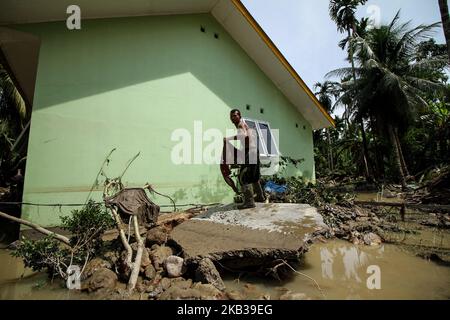 A man collects debris from a house damaged after a flood caused by ...