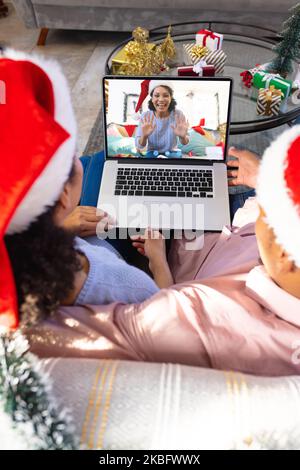Happy biracial woman having party at home with falling confetti making laptop video call, copy ...