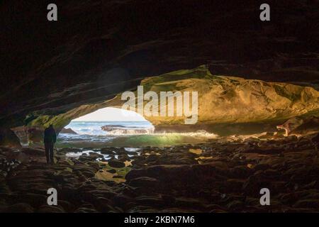 Tourist exploring Waenhuiskrans sea-cave, gazing towards the cave mouth ...