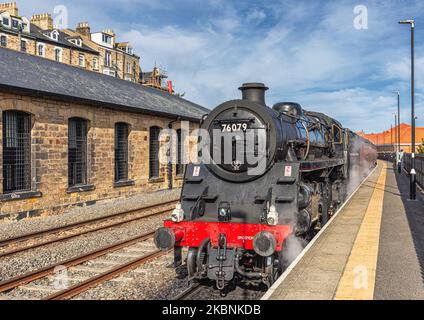 A polished black steam locomotive stands at a platform. Steam emits ...