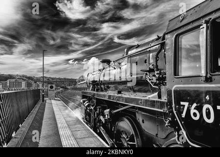 A polished black steam locomotive stands at a platform. Steam emits ...