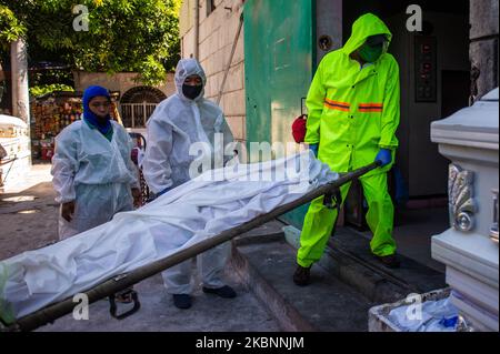 A funeral worker wearing a personal protective equipment (PPE) carrying ...