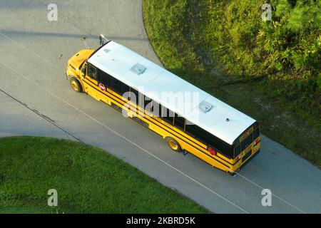 Aerial view of american yellow school bus driving on suburban street for picking up children for ...