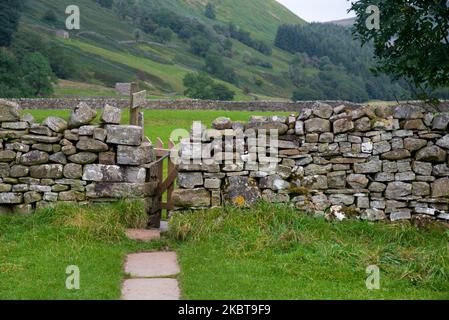 traditional stone gate or stile in a dry stone wall with flowers and ...