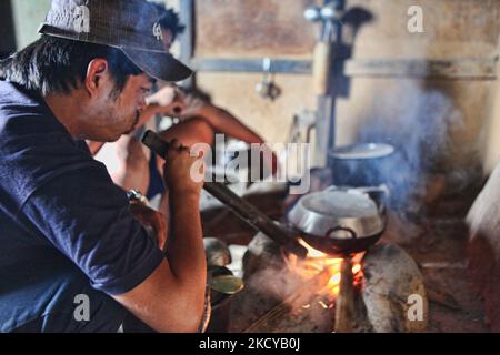 Lepcha man uses a bamboo tube to blow the embers in a traditional chula ...