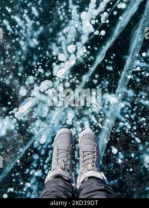 Fragile thin brittle ice underfoot. Male and female feet on ice. Cracks ...
