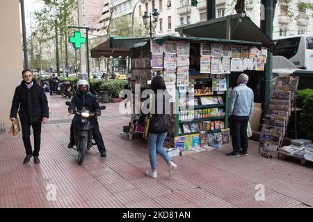 People are passing in front of a kiosk with newspapers in the center of ...