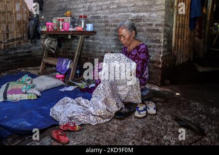 A worker applies wax to a batik using a canting tool prior to the ...