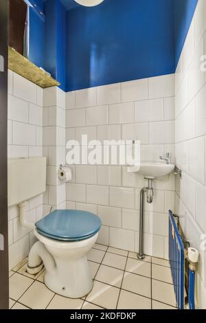 Flush toilet located between sink and shower in small tiled bathroom of ...