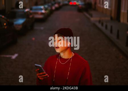 Asian boy in earphones using mobile phone while smoking at city street ...