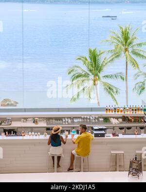 couple drinking cocktails at a bar during vacation looking out over the ...
