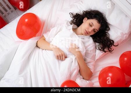 Brunette European girl sleeping on bed with red heart shape balloons ...